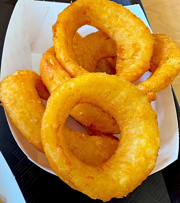 Golden, crispy onion rings that shatter satisfyingly between your teeth—the perfect supporting actor to the hot dog headliner in this culinary production.