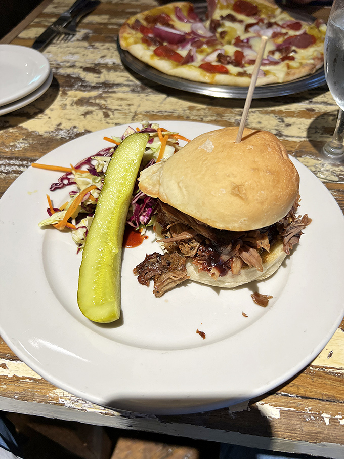 This pulled pork sandwich isn't messing around—it's bringing the smoke, the tang, and that pickle spear standing guard like a delicious sentinel.