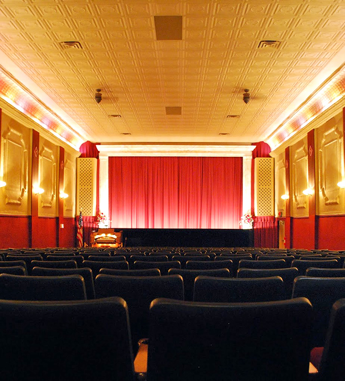 Empty before showtime, the auditorium reveals its true character—ornate wall panels, plush red seats, and that magnificent curtain promising cinematic escape.