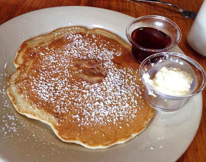 This pancake doesn't just sit on the plate—it commands attention with its golden hue and perfect dusting of powdered sugar.