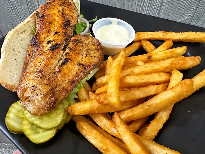This blackened fish sandwich isn't just lunch—it's a vacation on a plate, with perfectly seasoned fish, crisp pickles, and fries that deserve their own fan club.