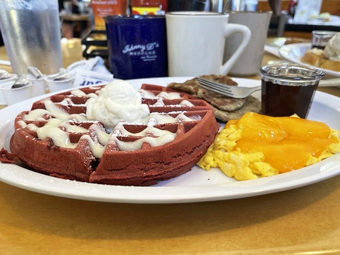 The red velvet waffle arrives like breakfast royalty, crowned with cream cheese drizzle and accompanied by perfectly scrambled eggs.