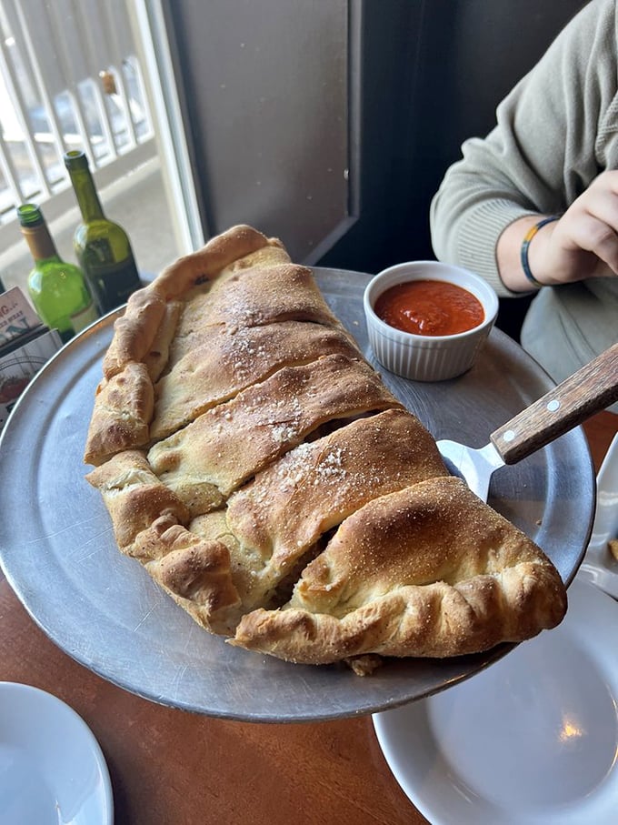 Behold the calzone in all its golden glory—a magnificent crescent of dough cradling treasures within, served with marinara for essential dipping.