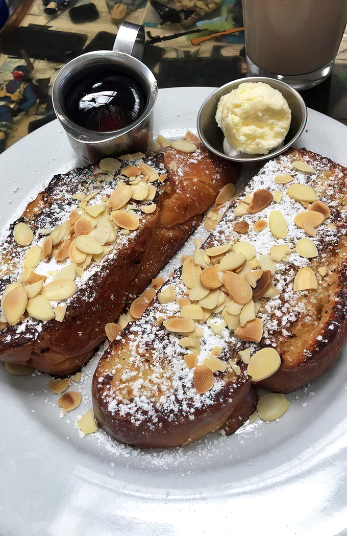 French toast that deserves its own fan club—golden-brown challah bread topped with powdered sugar and almonds, ready for its maple syrup bath.