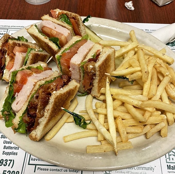 This club sandwich isn't playing around—triple-decker architecture holding crisp lettuce, juicy tomatoes, and generous meat portions with golden fries standing guard.