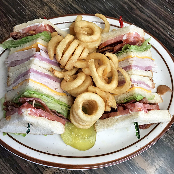 This club sandwich isn't just stacked—it's architectural. Three tiers of deli perfection surrounded by a moat of curly fries for proper dipping logistics.