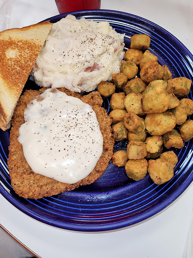 Southern comfort on a blue plate: country fried steak smothered in gravy alongside mashed potatoes and fried okra—a trifecta of down-home deliciousness.