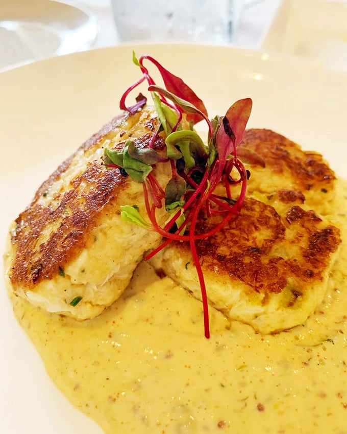 The legendary crab cake—more crab than cake—sits regally atop fresh asparagus, proof that sometimes the simplest preparations create the most profound flavors.