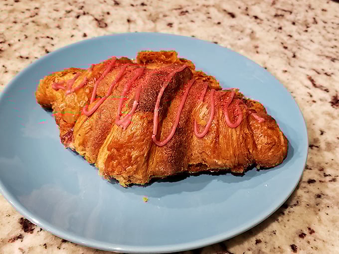 This isn't just a croissant—it's butter architecture, a flaky monument to French technique with a pink drizzle that says, "I'm fancy, but I don't take myself too seriously."