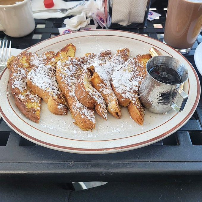 French toast that would make actual French people jealous. Golden, crisp-edged slices dusted with sugar and served with maple syrup in a metal pitcher—pure morning luxury.