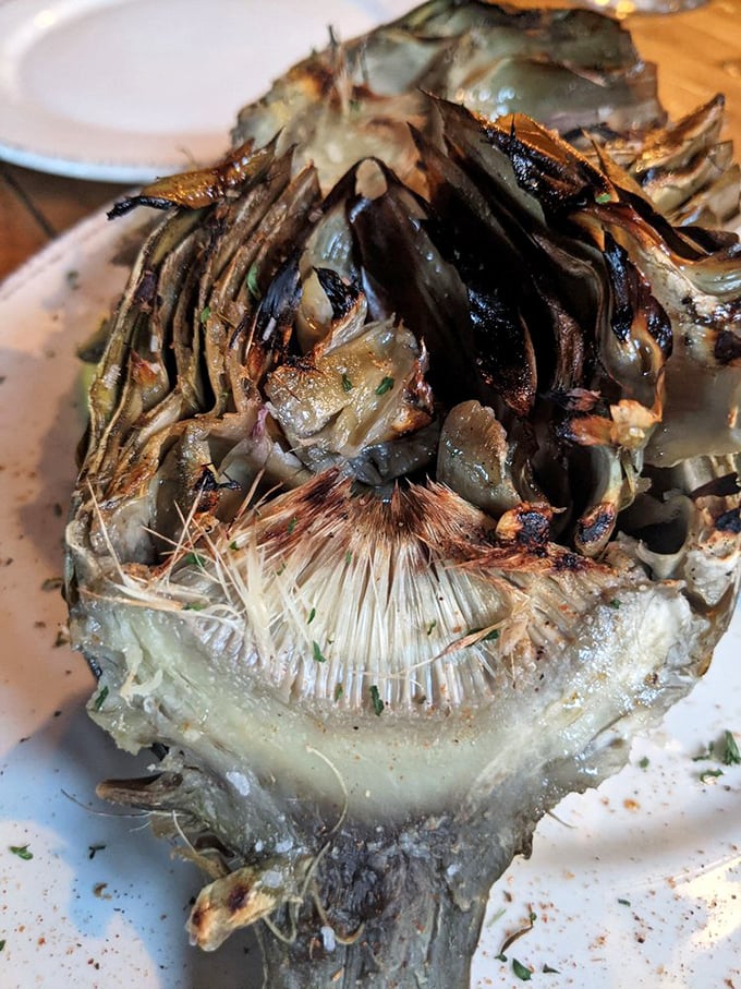 The grilled artichoke—nature's edible puzzle—transformed by fire and seasoning into something that makes you forget you're eating a vegetable.