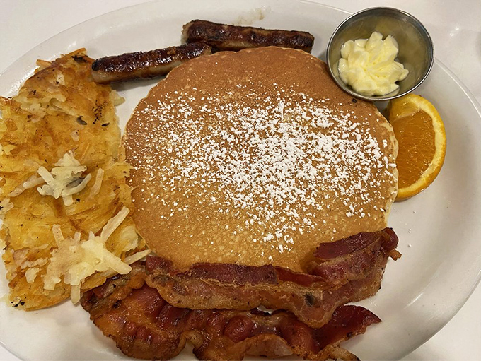 Pancakes dusted with powdered sugar snow, flanked by crispy bacon sentinels—breakfast doesn't get more American than this golden disc of morning joy.