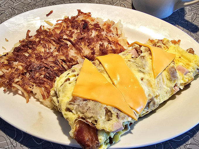 Omelet architecture at its finest—folded with precision around savory fillings and topped with perfectly melted cheese. The hash browns aren't playing second fiddle either.