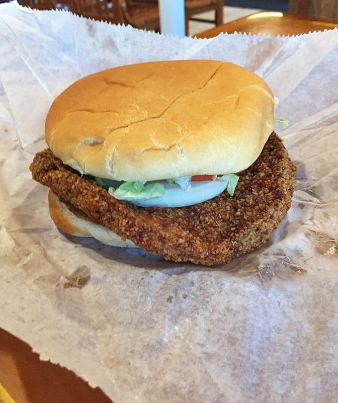 Indiana's iconic pork tenderloin sandwich in its natural habitat—crispy, golden, and hanging rebelliously over the edges of both bun and paper.