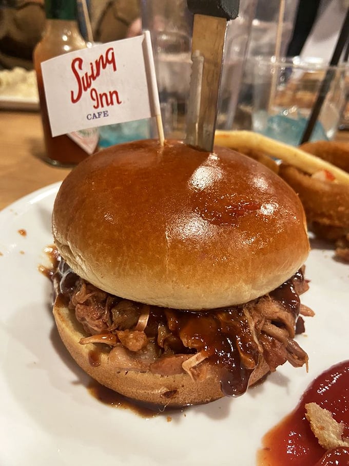Behold the pulled pork sandwich in all its glory – tender strands of smoky meat glistening with sauce, proudly flying the Swing Inn flag like a delicious victory banner.