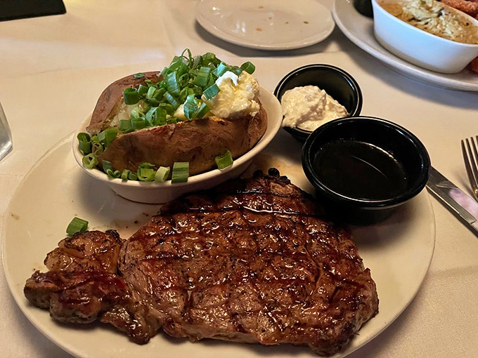 A rib eye steak with all the right accessories—loaded baked potato, savory sauces, and grill marks that should be framed in a museum.