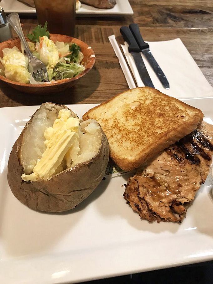 The perfect baked potato sits like a fluffy cloud next to its protein companion, both waiting patiently for you to decide which deserves the first bite.