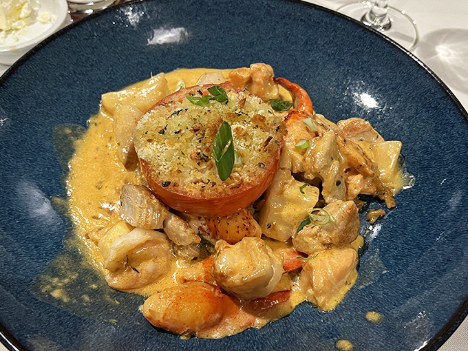 A seafood medley swimming in creamy sauce with a broiled tomato island—the kind of dish that makes you consider drinking the remaining sauce when no one's looking.