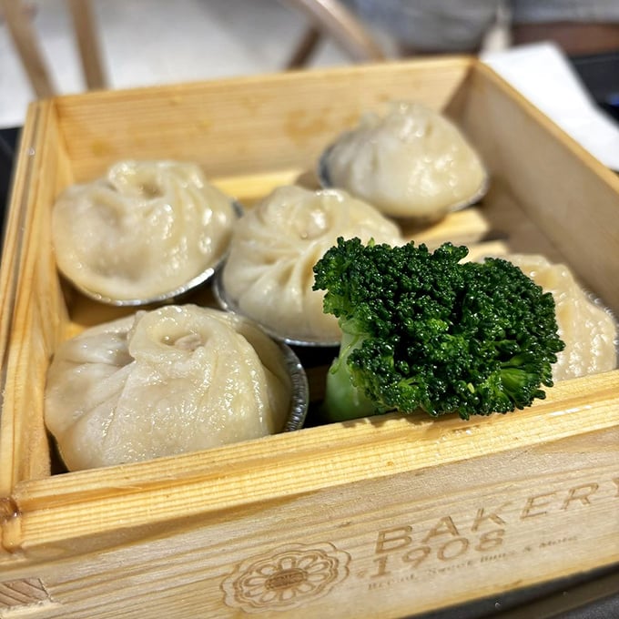 Soup dumplings sitting pretty in their wooden steamer basket—each one a self-contained flavor explosion waiting to happen. That broccoli garnish is living its best life.