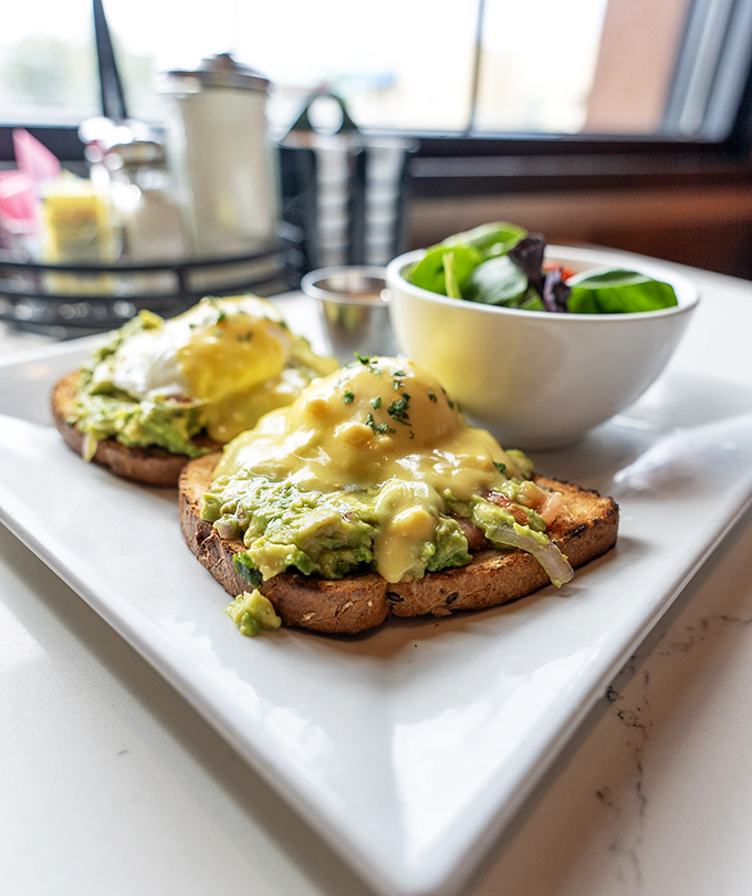 Avocado toast that even your skeptical uncle would approve of—perfectly poached eggs and hollandaise creating breakfast nirvana.