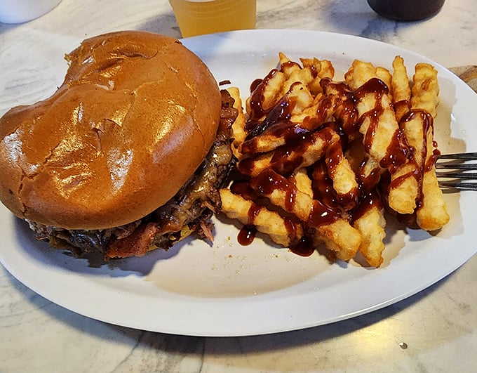 That burger isn't just sitting on the plate—it's posing for greatness. Those fries with BBQ sauce drizzle? They're the backup singers who could easily be the main act.