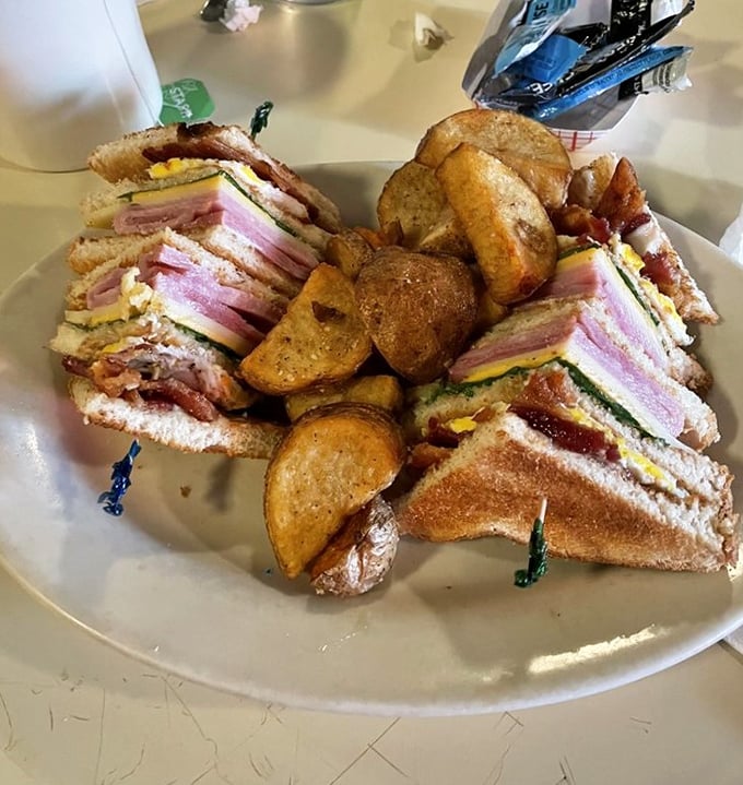 This isn't just a club sandwich—it's architecture. Layers of ham, bacon, and cheese create the skyscraper of sandwiches, with crispy potatoes standing guard.