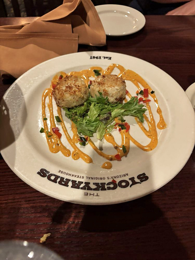 These golden crab cakes aren't just appetizers – they're the opening act to a magnificent meal, perched atop artistic swirls of sauce like culinary royalty.