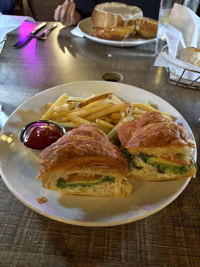 A sandwich that would make Neptune himself jealous—flaky croissant embracing fresh seafood with fries standing at attention.