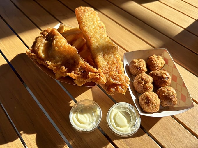 Fish and chips with a side of hush puppies—the holy trinity of fried goodness. Sunlight makes everything look like it was blessed by the fryer gods.