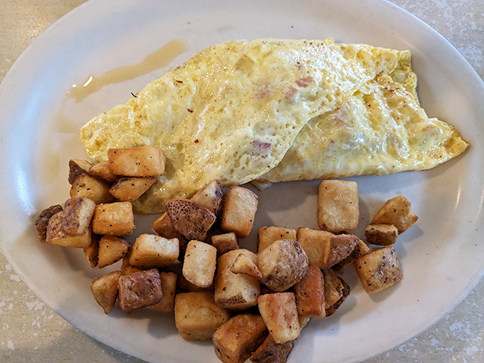 A perfectly executed ham and cheese omelet with home fries that achieve the culinary holy grail: crispy edges with pillowy centers.