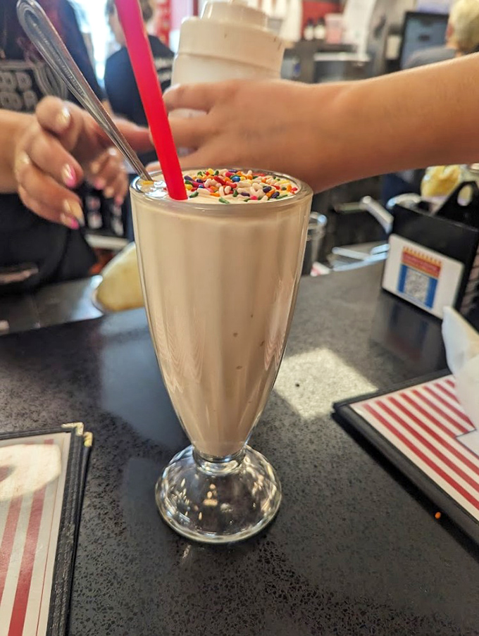 Sprinkles on top aren't just decoration—they're confetti celebrating this thick, creamy milkshake that requires serious straw commitment and zero regrets.
