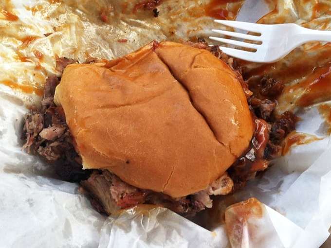 A pulled pork sandwich that doesn't need fancy presentation – just a soft bun struggling heroically to contain meat that's been smoking longer than some drivers have had licenses.