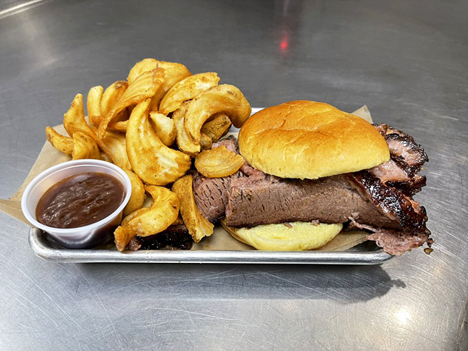 A brisket sandwich that doesn't hide behind fancy garnishes – just glorious smoke-kissed beef, a soft bun, and those golden curly fries.