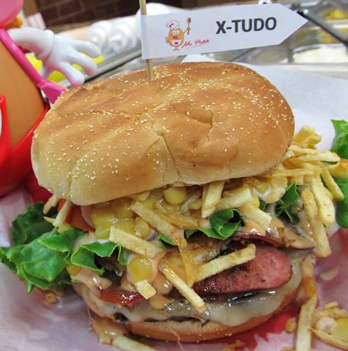 The X-Tudo burger defies gravity and conventional burger wisdom—stacked with potato sticks, ham, corn, and enough toppings to require a strategic eating plan.