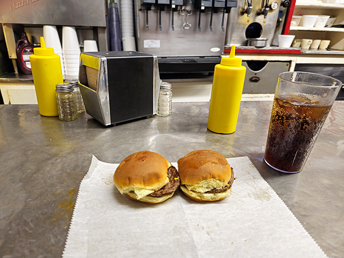 A plate of classic cheeseburgers awaits their destiny on the stainless steel counter—simple, honest, and exactly what you're craving at 2 AM.
