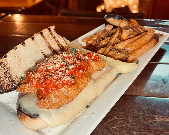 A sandwich that deserves its own ZIP code – crispy chicken parmesan nestled in melted cheese with perfectly golden fries standing guard nearby.