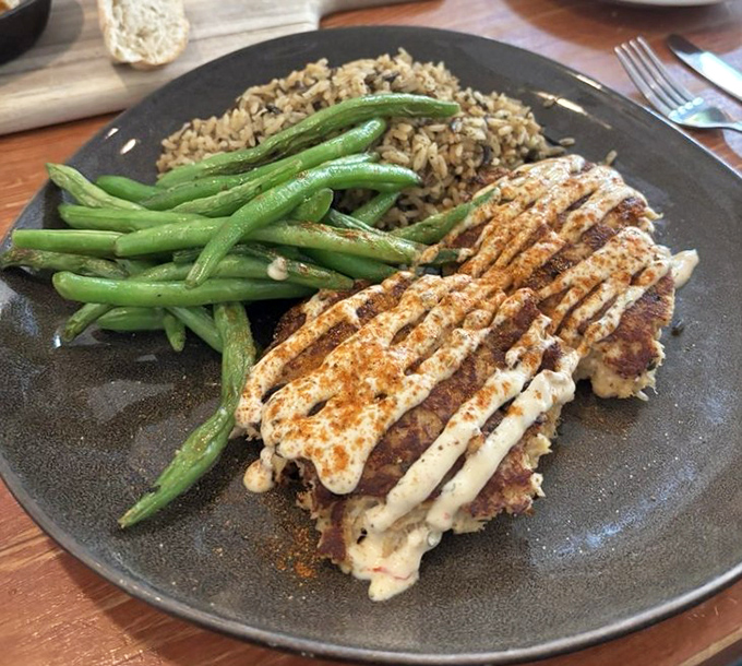 The legendary crab cakes that launched a thousand return visits, flanked by vibrant green beans and rice that refuses to be mere sidekicks.