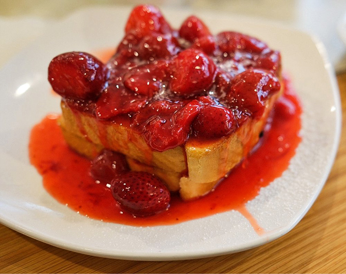 French toast turned dessert masterpiece—strawberries swimming in their own sweet juices atop golden bread islands. Morning bliss defined.