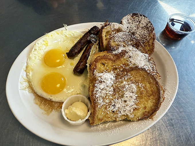 French toast that's had a proper education—powdered sugar, sunny-side-up eggs, and sausage links that snap when you bite them. Breakfast doesn't get more photogenic than this.