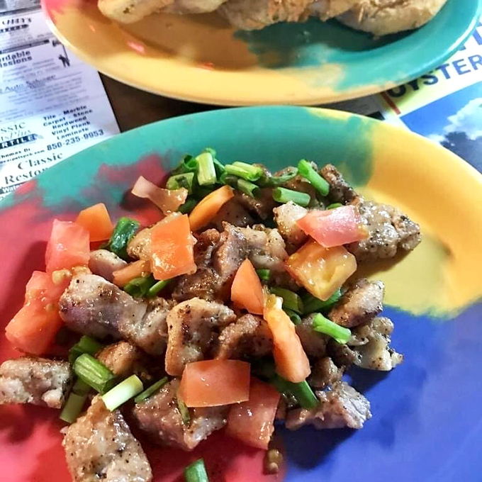 This colorful plate showcases what appears to be seasoned fish or seafood topped with fresh tomatoes and green onions—simple ingredients elevated by expert preparation.