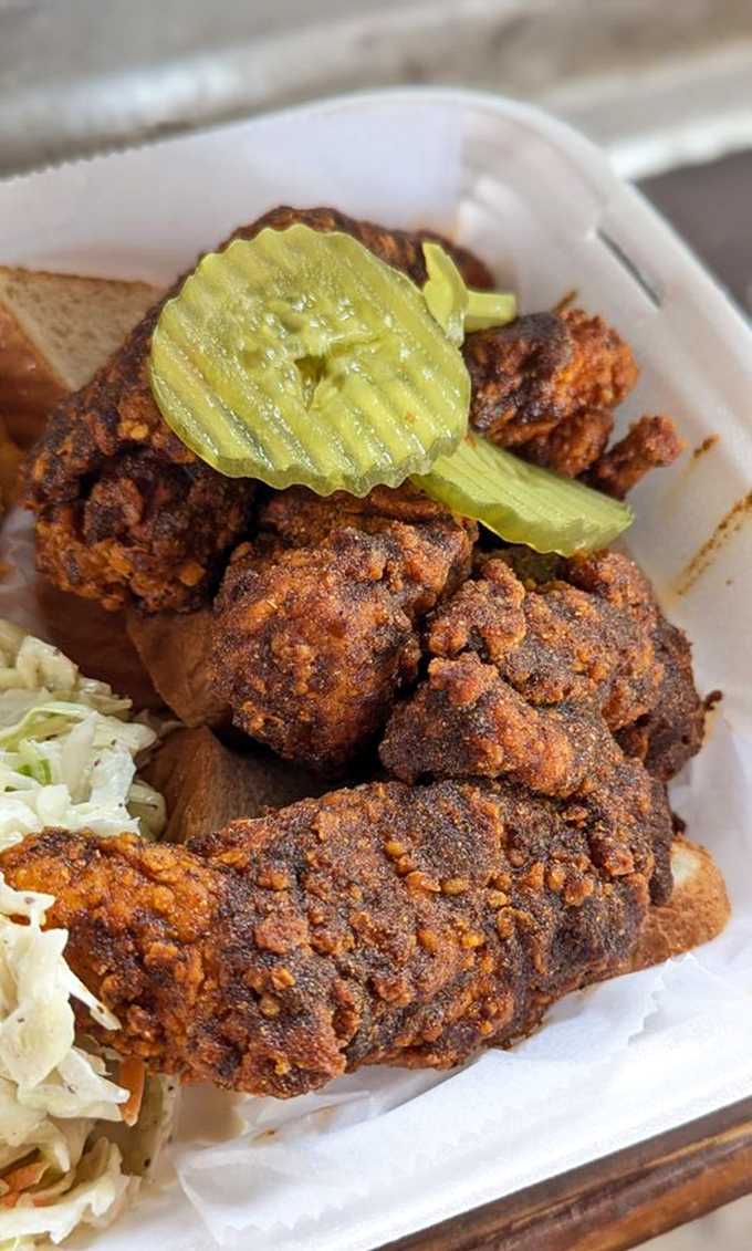 Traditional hot chicken served on white bread with pickle chips—a time-honored Nashville combination that's both fire and comfort. The coleslaw stands by, ready for emergency cooling duties.