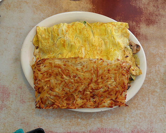 An omelet that's seen things—namely hash browns that have achieved the perfect crisp-to-tender ratio. Breakfast nirvana on a simple white plate.
