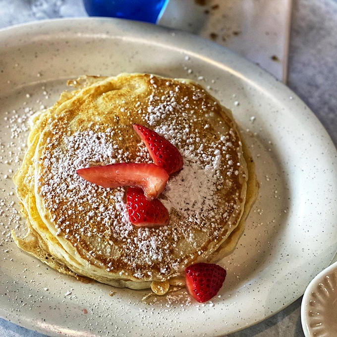Pancakes so perfectly golden they belong in Fort Knox, with strawberries standing guard like tiny red sentinels of sweetness.