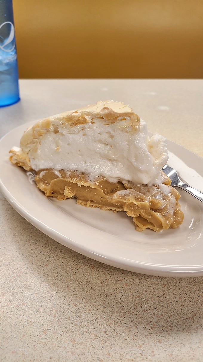 Meet the peanut butter pie that has launched a thousand return visits—creamy filling beneath a cloud of whipped topping with just enough texture to make you slow down.