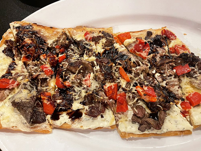 The flatbread arrives like a savory mosaic of tender beef, roasted peppers, and melted cheese—a shareable masterpiece that rarely gets shared.