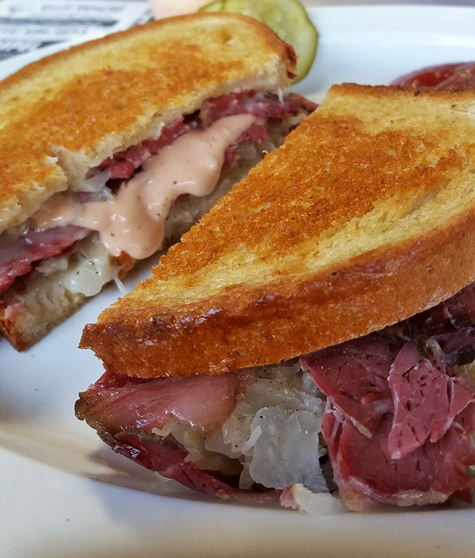 The legendary Reuben—architectural perfection between bread. Each layer visible like geological strata of deliciousness, with Russian dressing lava.