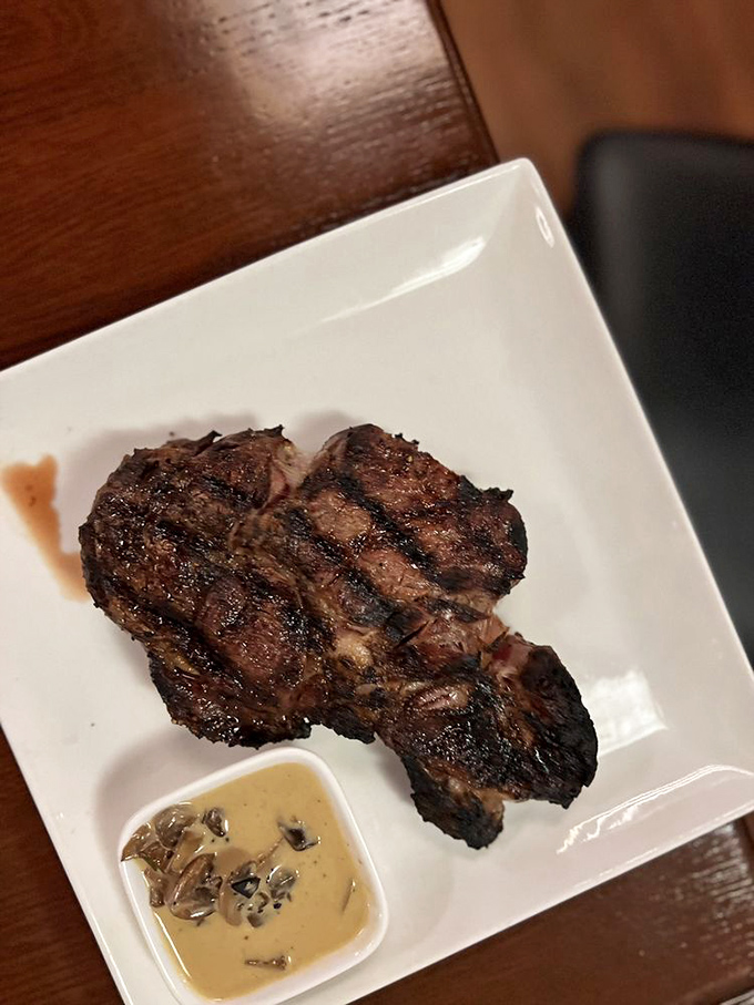 Behold the ribeye in its natural habitat: perfectly charred exterior, juicy interior, and a side of mushroom sauce for good measure.