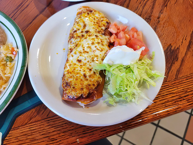 This isn't just any enchilada—it's a cheese-blanketed envelope delivering a love letter to your taste buds, with diced tomatoes and shredded lettuce for company.