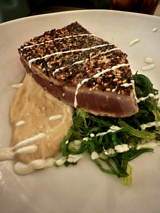 Sesame-crusted tuna that's seared just right—still blushing pink inside—resting on a bed of greens like it's taking a well-deserved vacation.