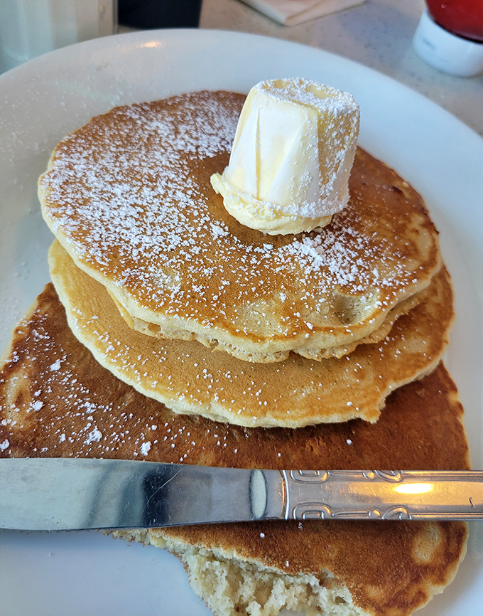 Pancakes stacked higher than Florida's humidity, crowned with a melting butter hat and powdered sugar snowfall. Your diet plan just called—it's taking the day off.